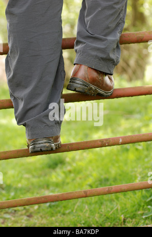 Walker climbing over metal gate UK Stock Photo - Alamy