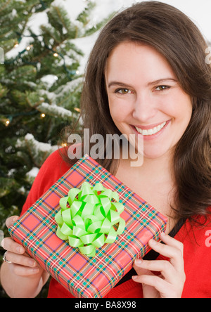 Woman with Christmas tree holding gift on blue background Stock Photo ...