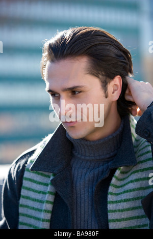 Young man standing outdoors in a park, smiling and looking away ...