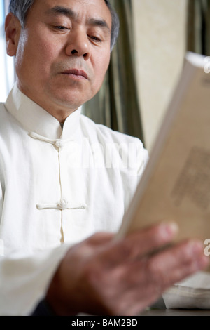 The senior Asian man reading the books at the desk with the blue ...