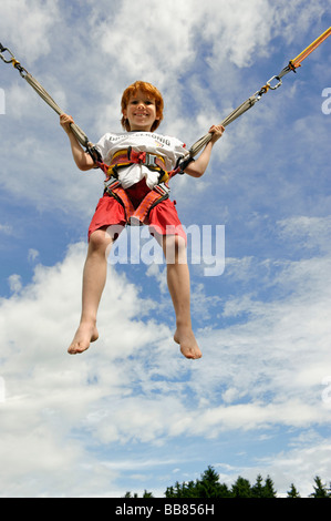 Boy jumping on a bungee trampoline and flying in the air in the autumn ...
