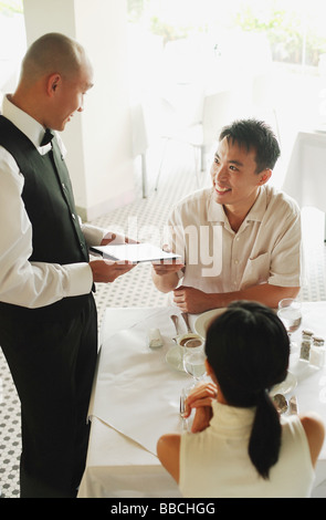 Couple in restaurant, man handing menu back to waiter Stock Photo - Alamy