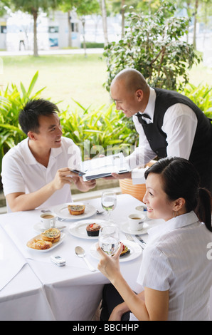 Couple in restaurant, man handing menu back to waiter Stock Photo - Alamy