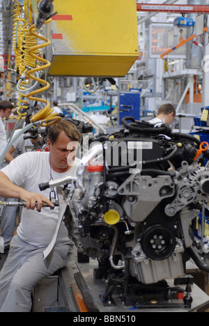 Employees of the Audi Factory work at an engine on the production line ...