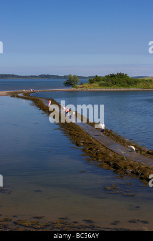 tourists walking concrete causeway at low tide to rough island from ...