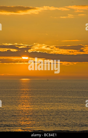 Sun setting over calm sea with gentle waves on sandy beach, wide view ...