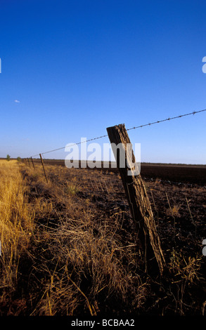 Farm fields and a crooked fence post and barbed wire fence at sunset ...