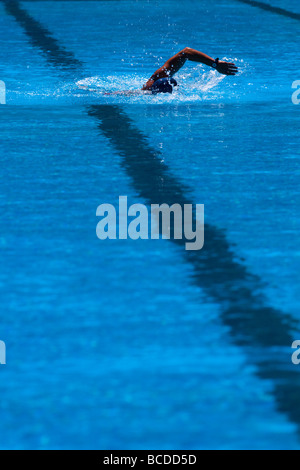 A lone man swimming laps in a wetsuit using hand paddles in an ocean ...