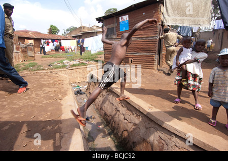 Children jumping over open sewer in African slum Stock Photo - Alamy