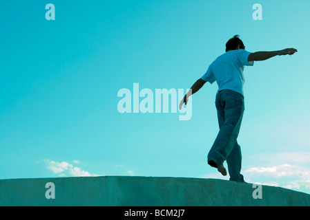 Man standing on ledge with arms out, leaning forward, rear view Stock ...