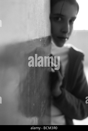 Preteen girl looking around corner of wall, cropped Stock Photo - Alamy