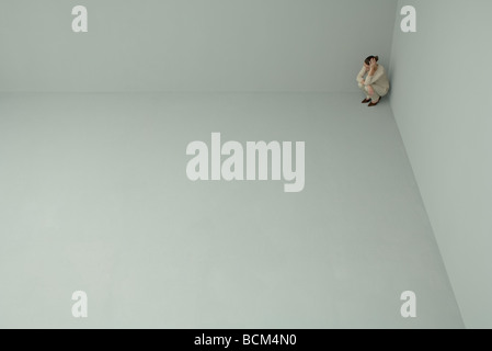 Woman crouching in corner of large empty room, mid-distance, high Stock ...
