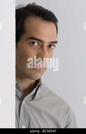 Man looking around corner of wall, portrait Stock Photo - Alamy