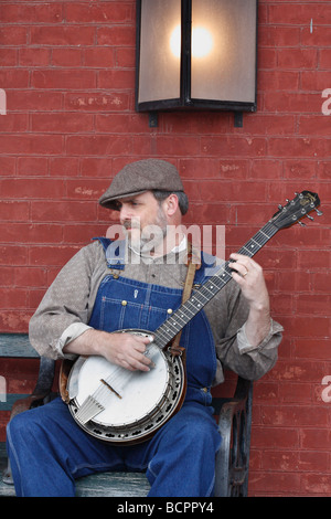 A busker playing banjo mandolin on the city street sitting on the bench ...