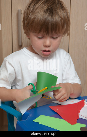 young boy cutting modelling paper with small scissors sitting at small ...