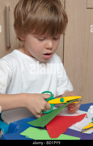 young boy cutting modelling paper with small scissors sitting at small ...