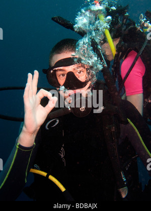 A scuba diver making the OK sign while sitting on the edge of a Stock ...