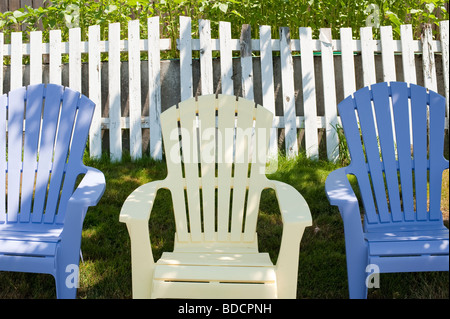 Lawn chairs lined up under the shade of a tree with white picket fence ...