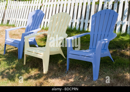 Lawn chairs lined up under the shade of a tree with white picket fence ...