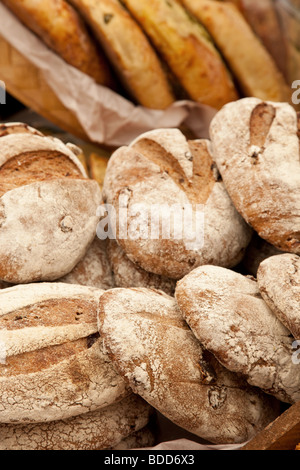 A loaf of brown bread with grains of cereals on a wooden cutting board ...