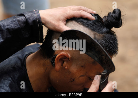 Traditional Basha hair shaving with a sickle on a man with a hair bun ...