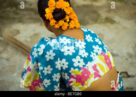 A South Indian maid sweeps a courtyard with flowers in her hair ...