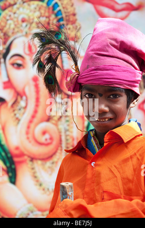 Indian beggar boy with musical instrument against a poster of hindu ...
