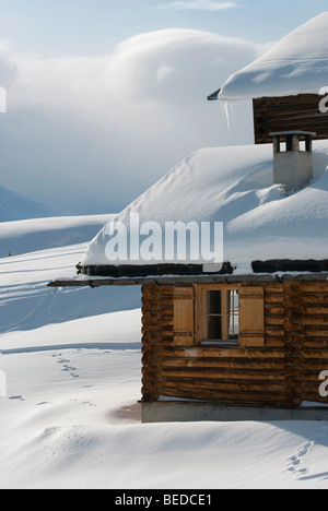 A log cabin with a snow covered roof. The cabin has a porch with a ...