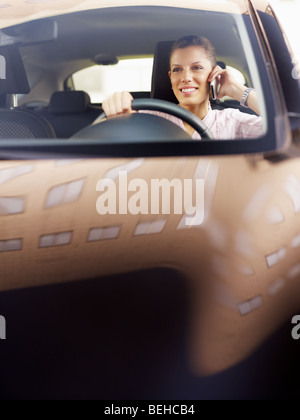 Woman driving and smiling while talking on a mobile phone in a car ...