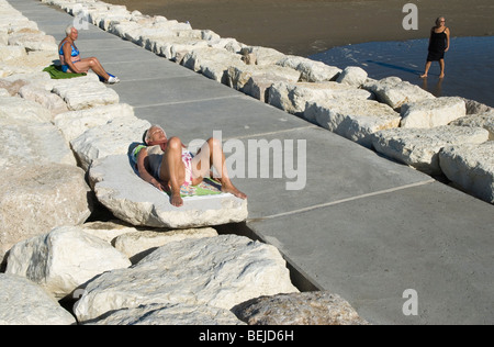 Old lady in bathing costume and swimming hat on pebbled beach in ffront ...