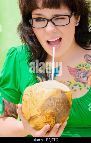 Black young woman winking while drinking coconut water isolated over ...