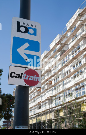 A low angle view of BART and Caltrain road signs by a scaffolded condo ...