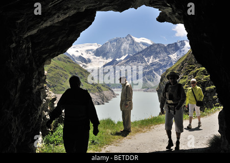 A group of people are walking through a cave with a blue railing. The ...