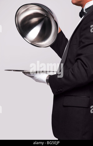 Butler lifting the cloche from a silver serving tray to reveal a house ...