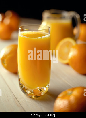 A glass pitcher of juice with fresh orange fruits on stone background ...