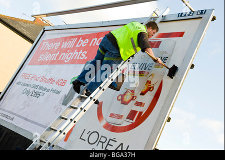 Worker up ladder with long handled brush pasting advertising poster on ...