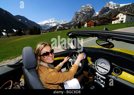 A smiling woman driving a convertible Mini Cooper through the ford ...