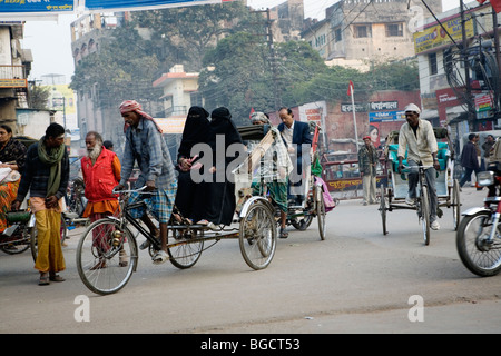 Muslim women travel by rickshaw in crowded street scene in city of ...