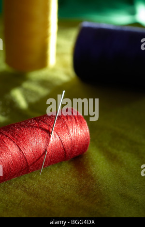 Cotton reel with red thread and sewing needle Stock Photo - Alamy