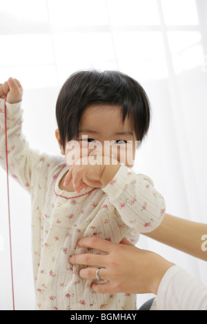 Baby holding string and covering mouth with hand Stock Photo - Alamy
