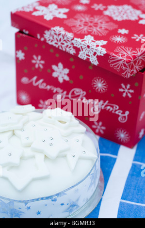 A red Merry Christmas gift box with a gold bow on a white table beside ...