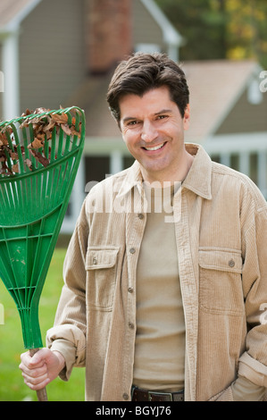 Man holding rake with fallen autumn leaves in the yard Stock Photo - Alamy