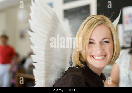 Woman wearing angel wings sitting on ledge, head down, hair obscuring ...