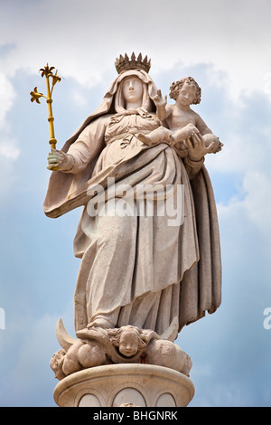 Statue of the Virgin Mary with infant Jesus and painting behind ...