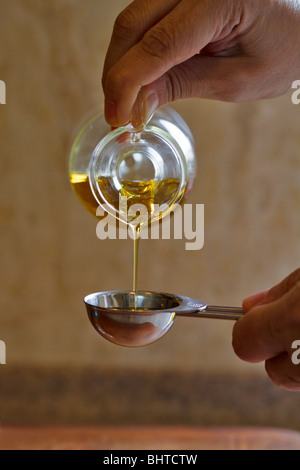 Pouring olive oil into a measuring spoon, measuring a tablespoon of oil ...