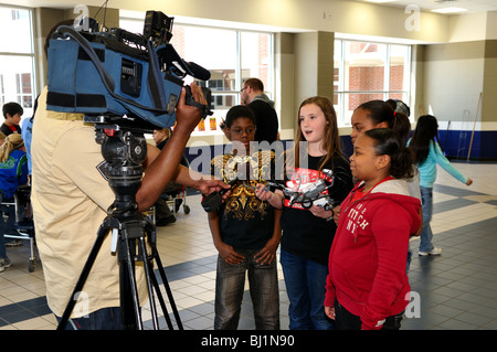 A group of school kids are interviewed by a TV reporter during a ...
