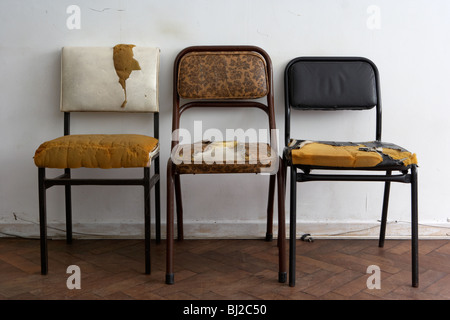 three old dirty worn out chairs against a white wall in a run down ...
