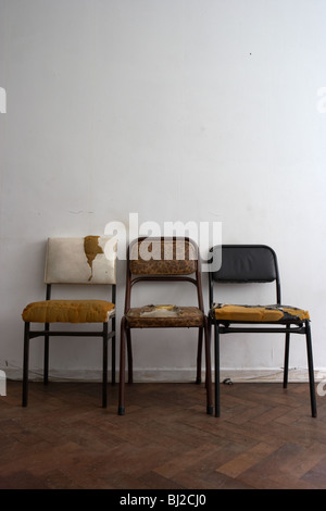 three old dirty worn out chairs against a white wall in a run down ...
