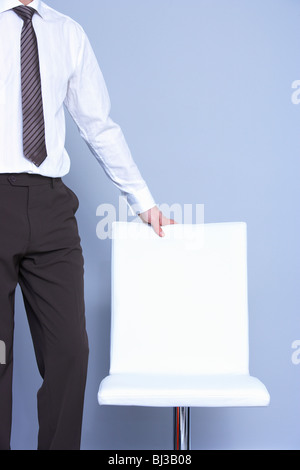 Businessman standing next to office chair, adjusting his glasses ...