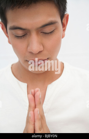 Young hispanic man praying with hands together in thoughtful pose ...